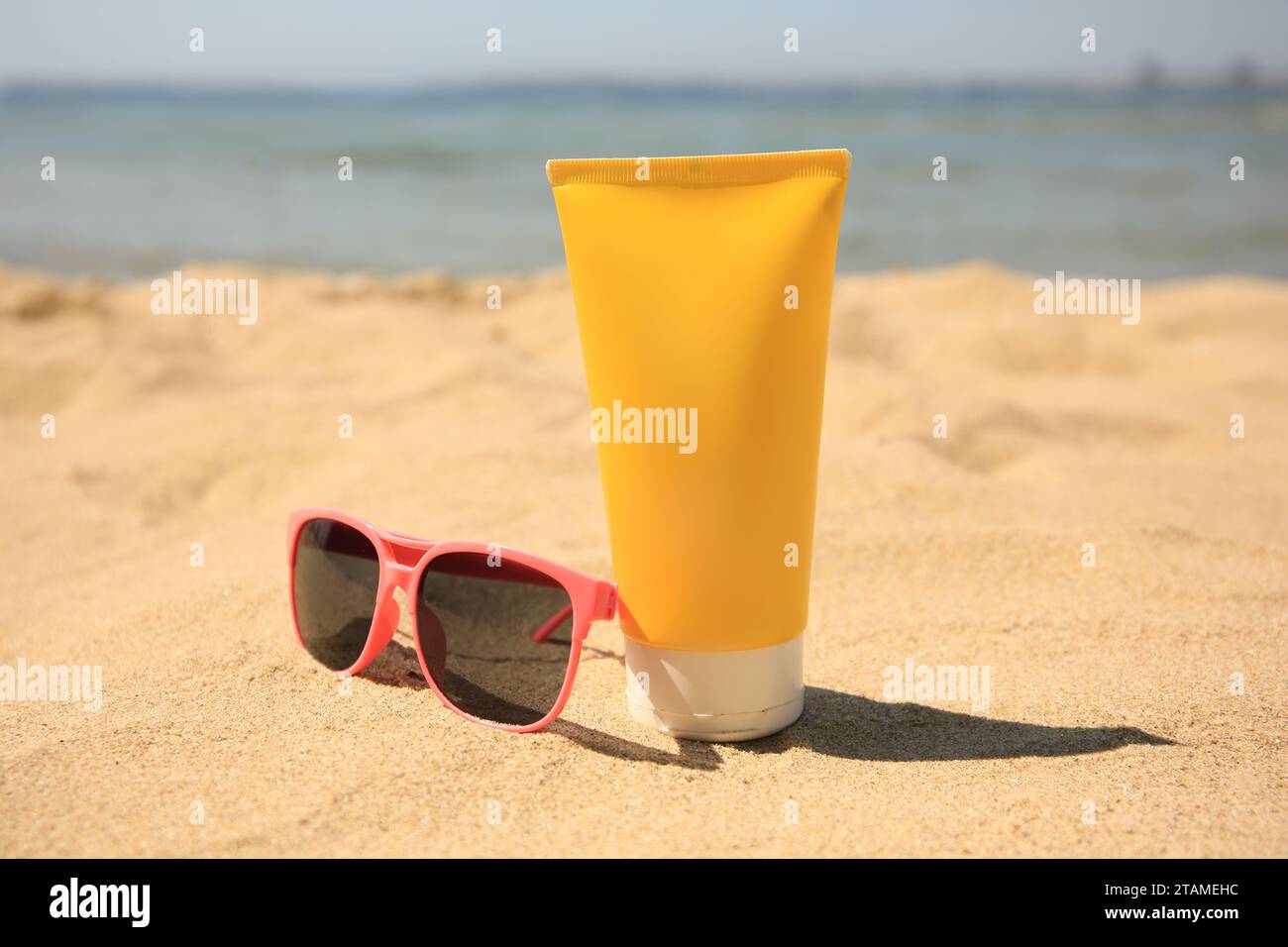 Tube of sunscreen and sunglasses on sandy beach. Sun protection care ...