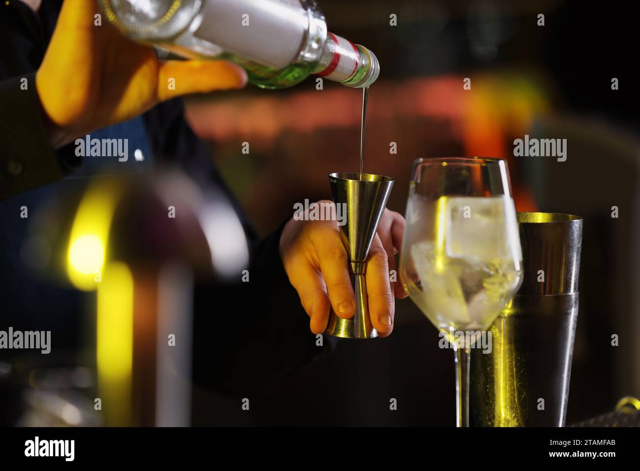 Cocktail making. Bartender pouring alcohol from bottle into jigger on blurred background ...