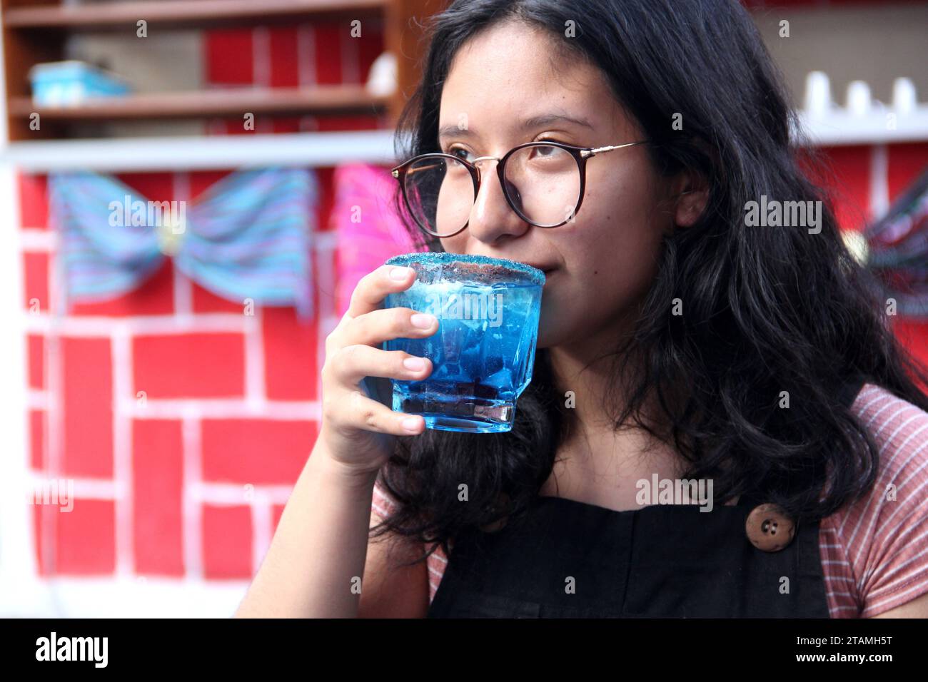 Young brunette Latina teenager woman drinks a blue colored Azulito ...