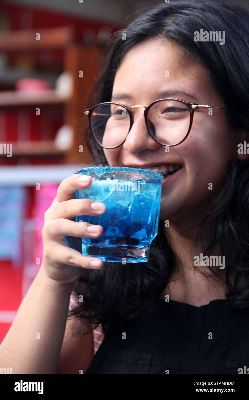 Young brunette Latina teenager woman drinks a blue colored Azulito ...