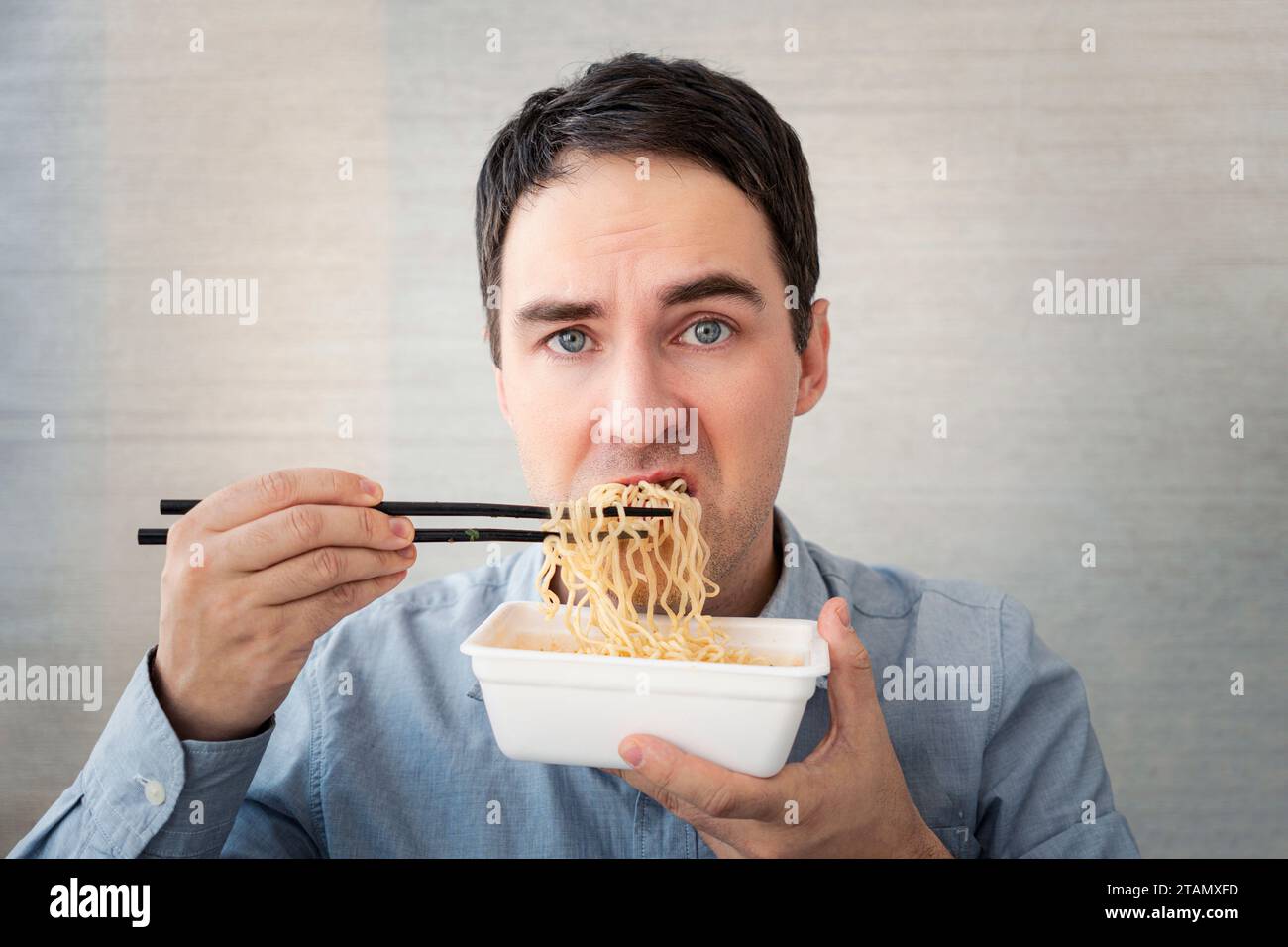 a young man in a blue shirt is eating noodles from a box with a ...