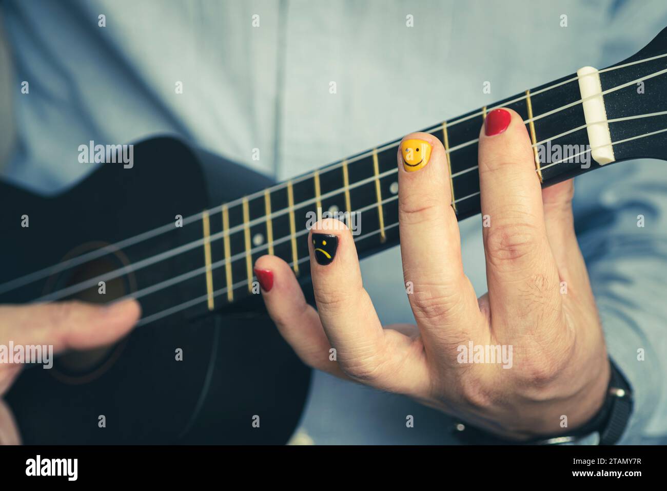 A musician with painted fingernails plays a ukulele in close-up. A ...