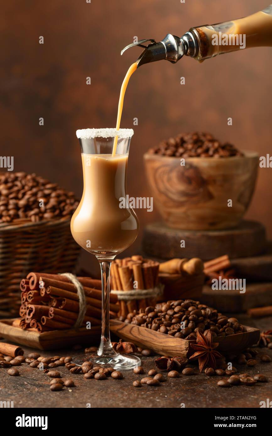 Irish cream and coffee liqueur is poured from a bottle into a glass. Coffee beans, cinnamon ...