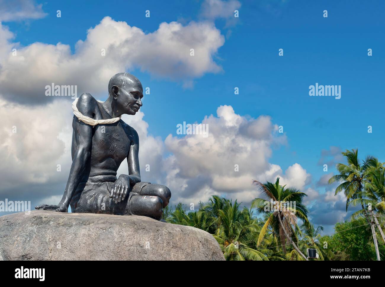 A statue of a seated Mahatma Gandhi on a rock anf against a blue sky ...