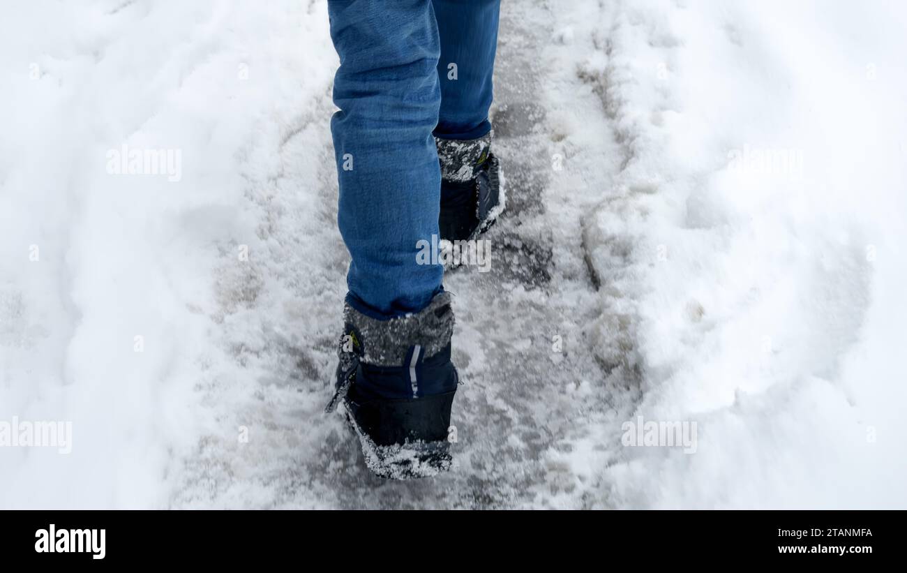 Closeup of child's feet in snow boots walking on road covered with snow ...