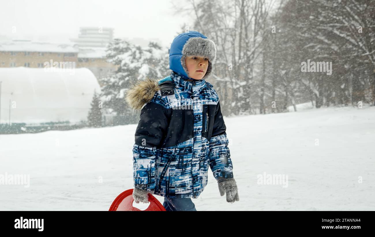 A smiling boy carries his sleds up a snow-covered hill, ready for an ...