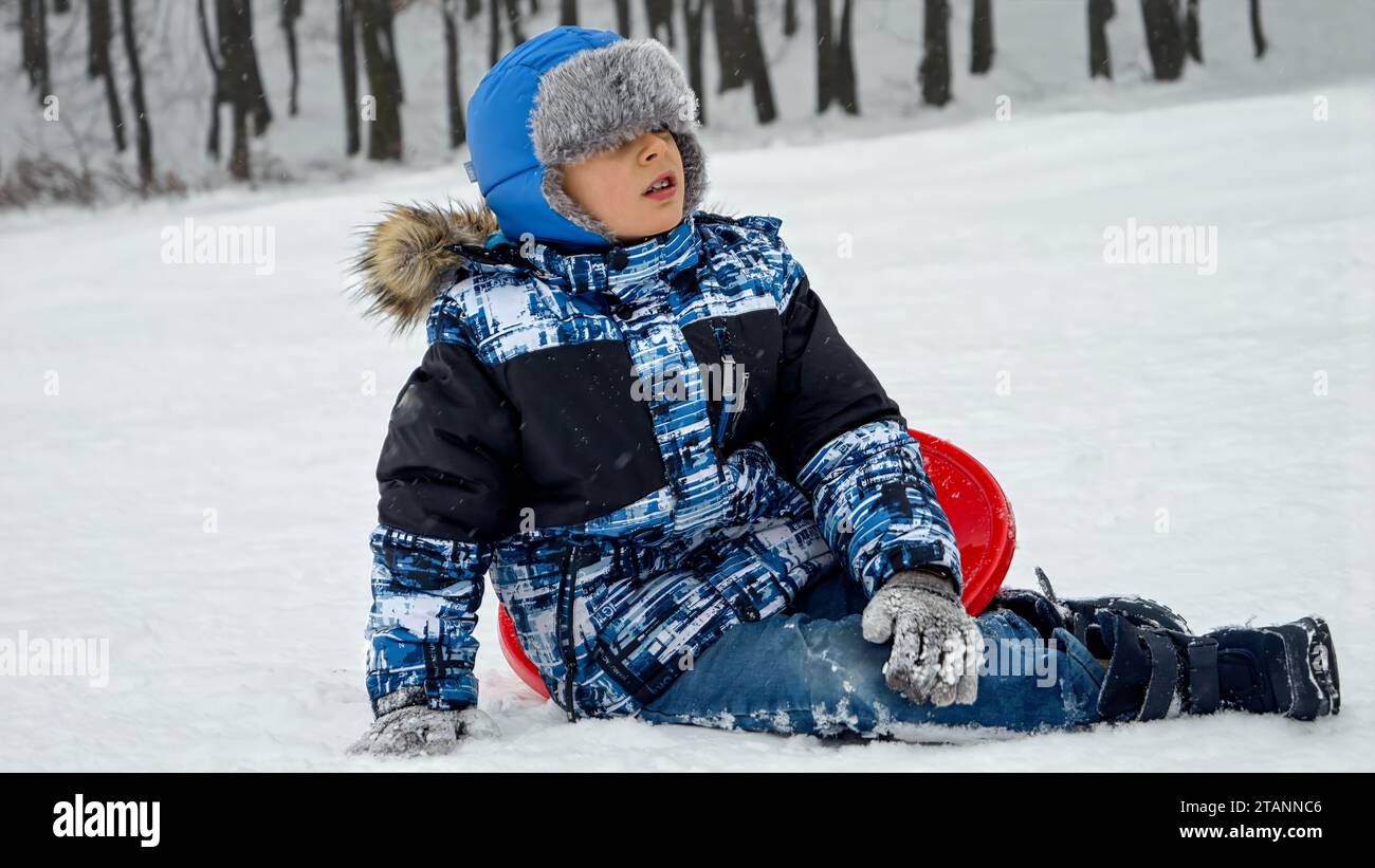 Little boy lying on snow and rubbing his hurting leg after falling down ...