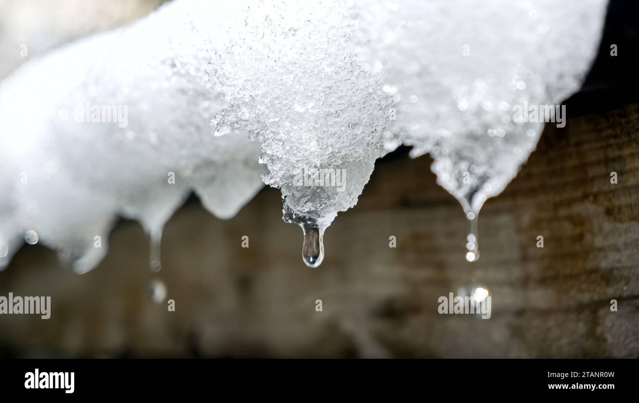 Close-up shot of water droplets falling from icicles on a rooftop ...