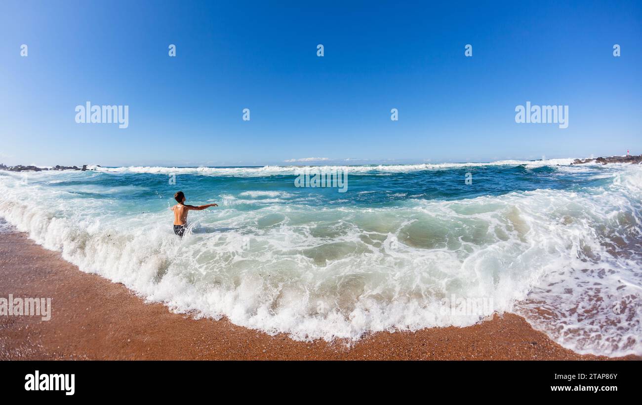 Young Caucasian boy on beach sand enters ocean into crashing shore ...