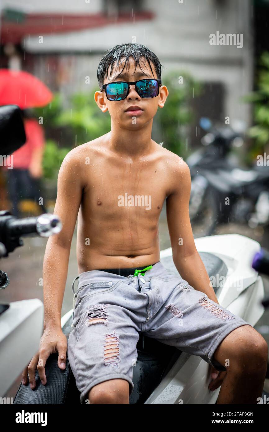 A cool little Filipino boy strikes a cool pose with his shades on in the rain in Tondo, Manila ...