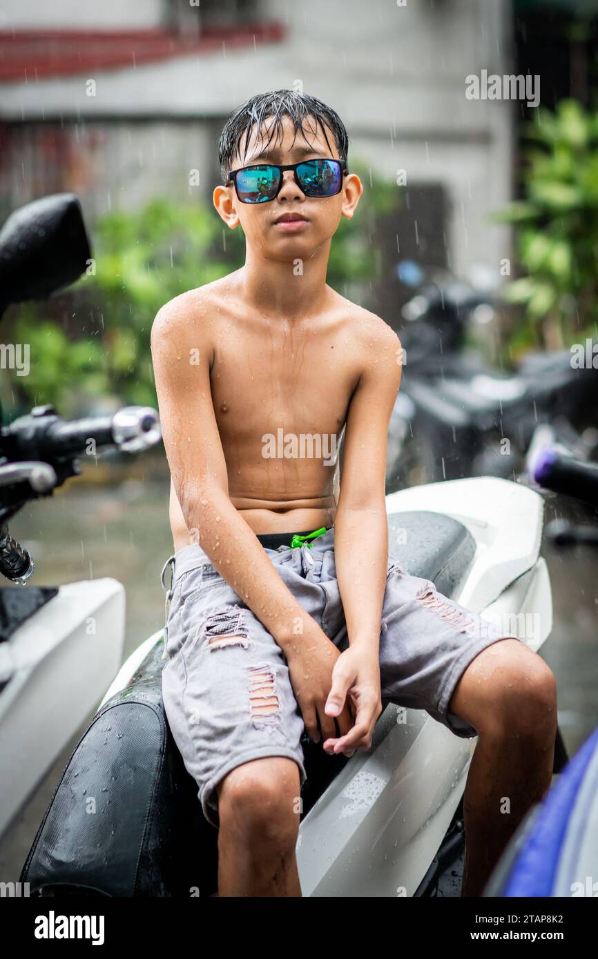 A cool little Filipino boy strikes a cool pose with his shades on in the rain in Tondo, Manila ...