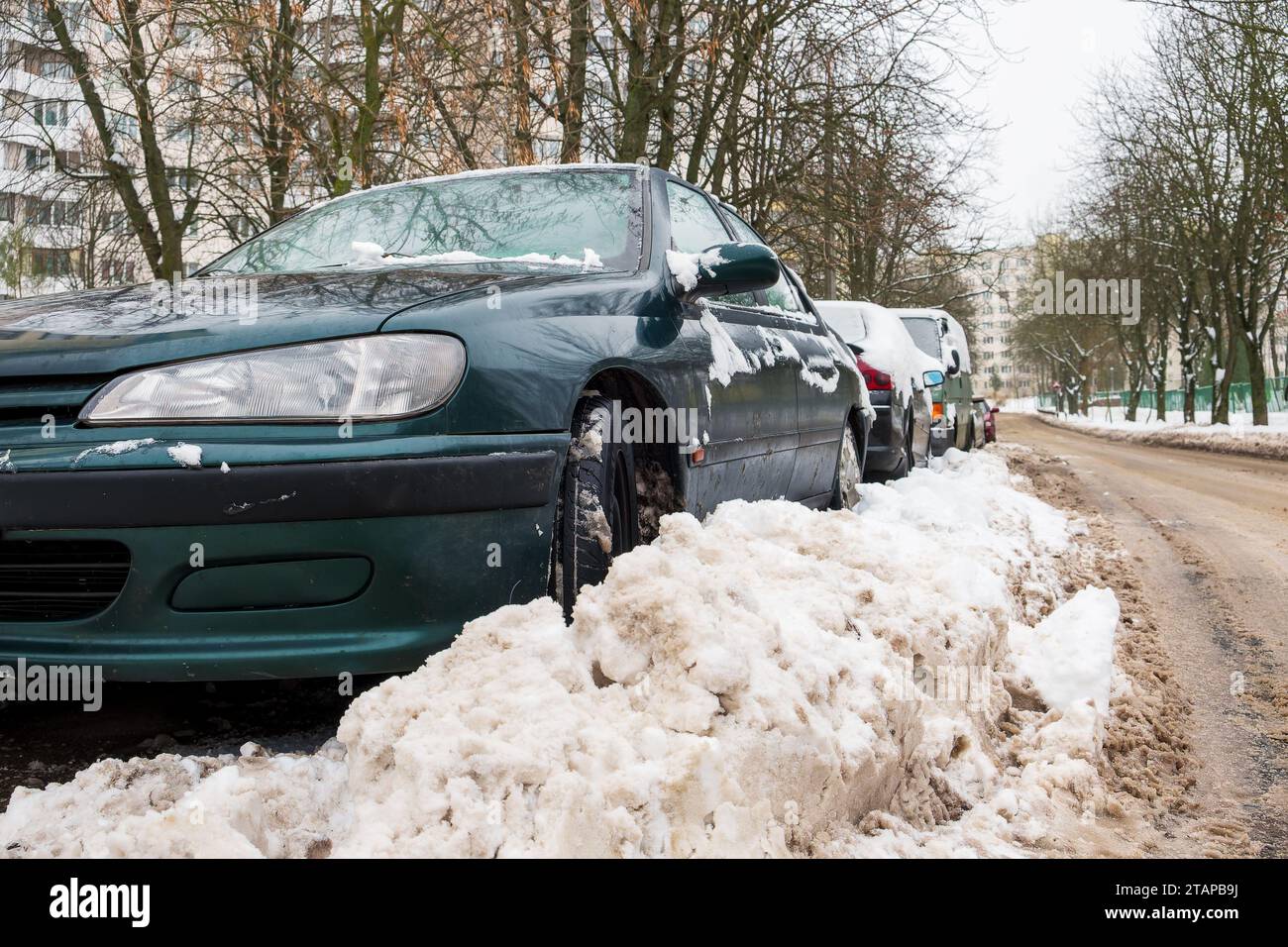 Winter. The road is covered with snow. Cars parked along the roadside ...