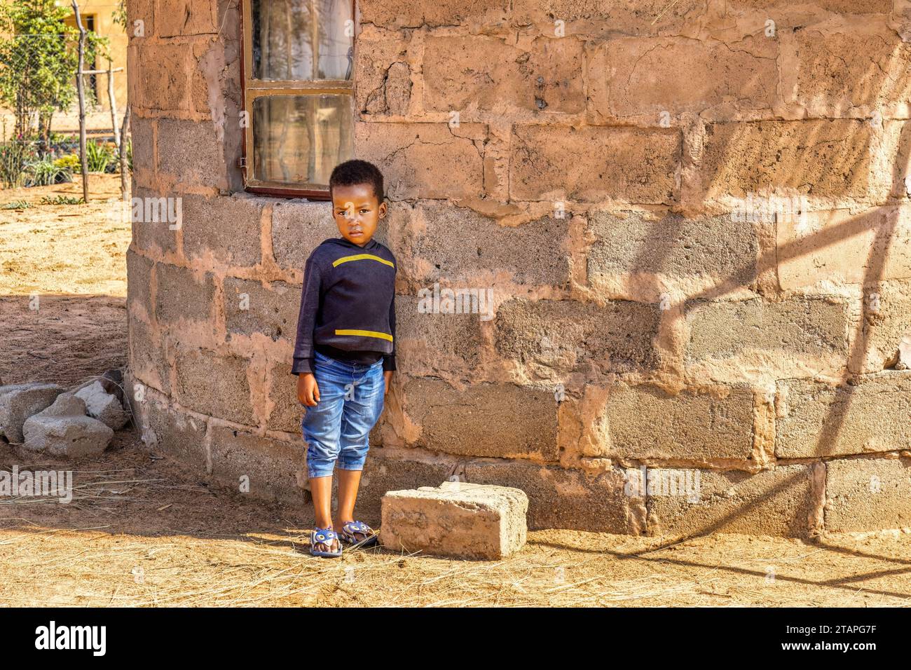 village african child standing by the house wall in the yard in a sunny ...