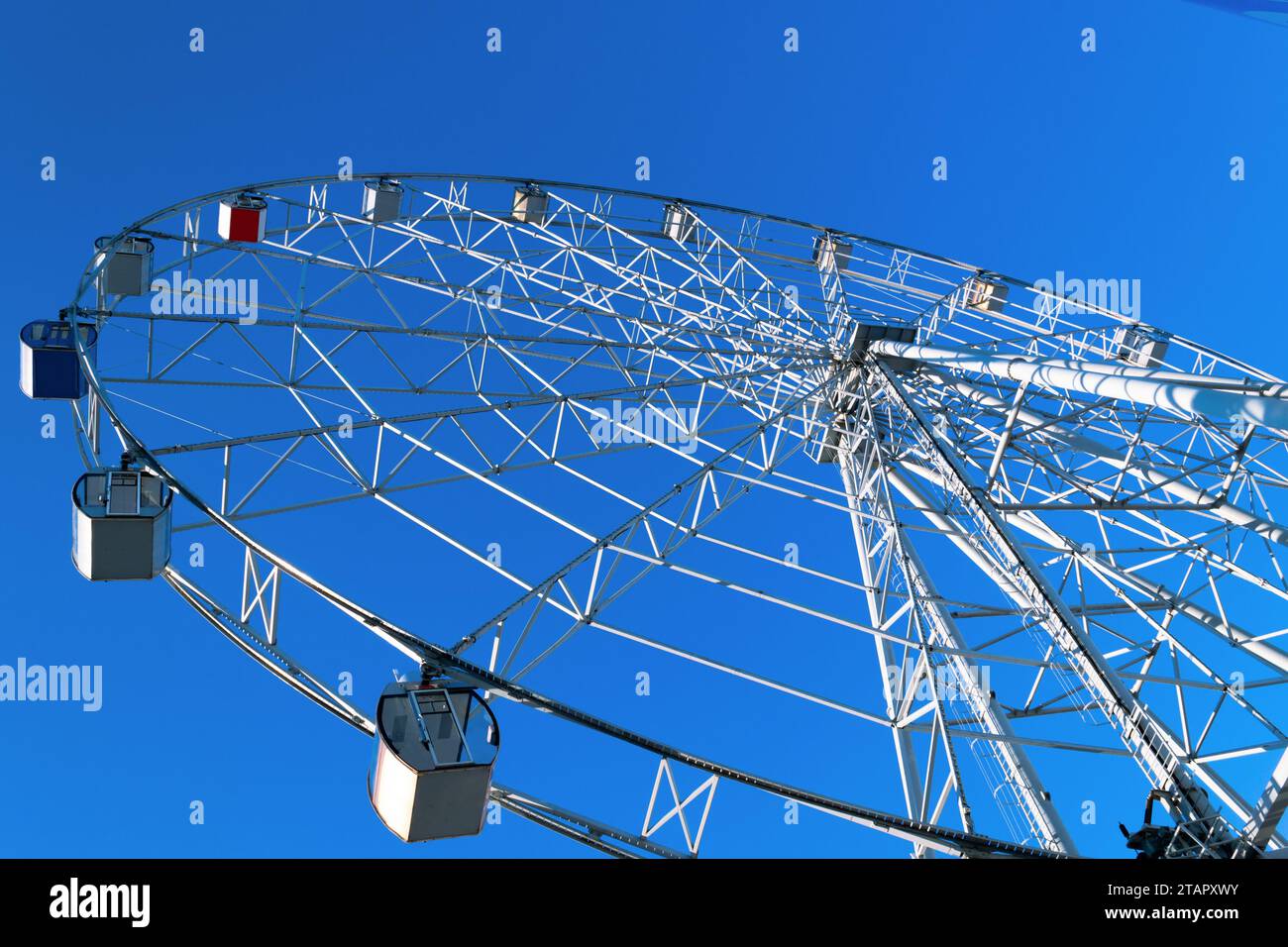 A white round Ferris wheel with booths against a blue daytime sky. Shot ...