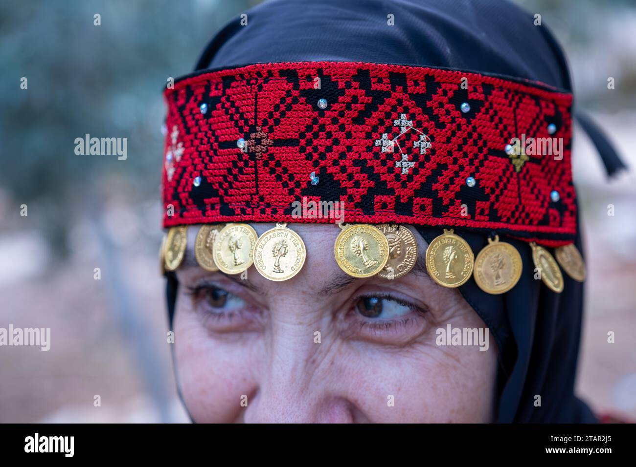 A Palestinian woman head dress in red and black with golden accessories ...