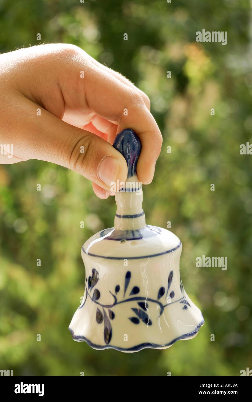 Hand holding a ceramic bell on a green background Stock Photo - Alamy