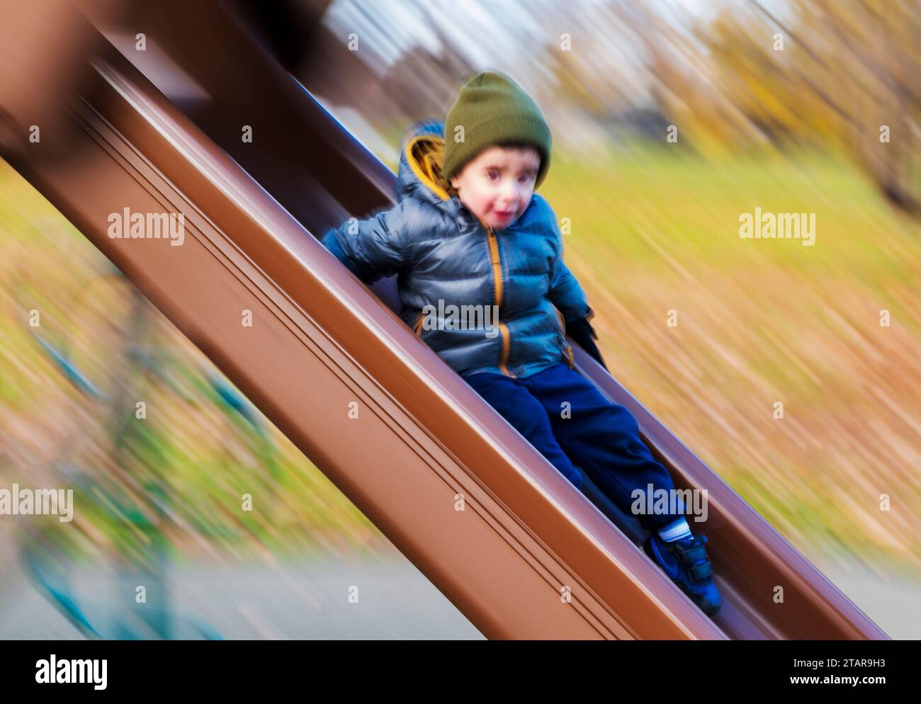 Autumn pan motion blur of young boy descending playground sliding board ...