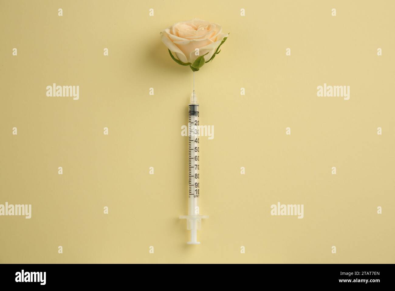 Medical syringe and beautiful rose on pale yellow background, top view ...