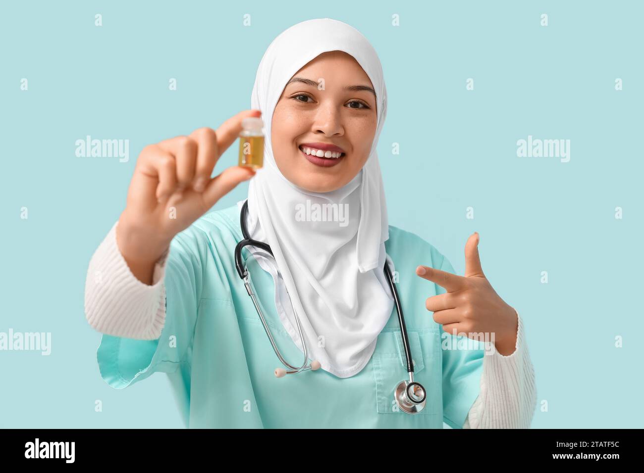 Female Muslim doctor in hijab pointing at ampule on blue background ...