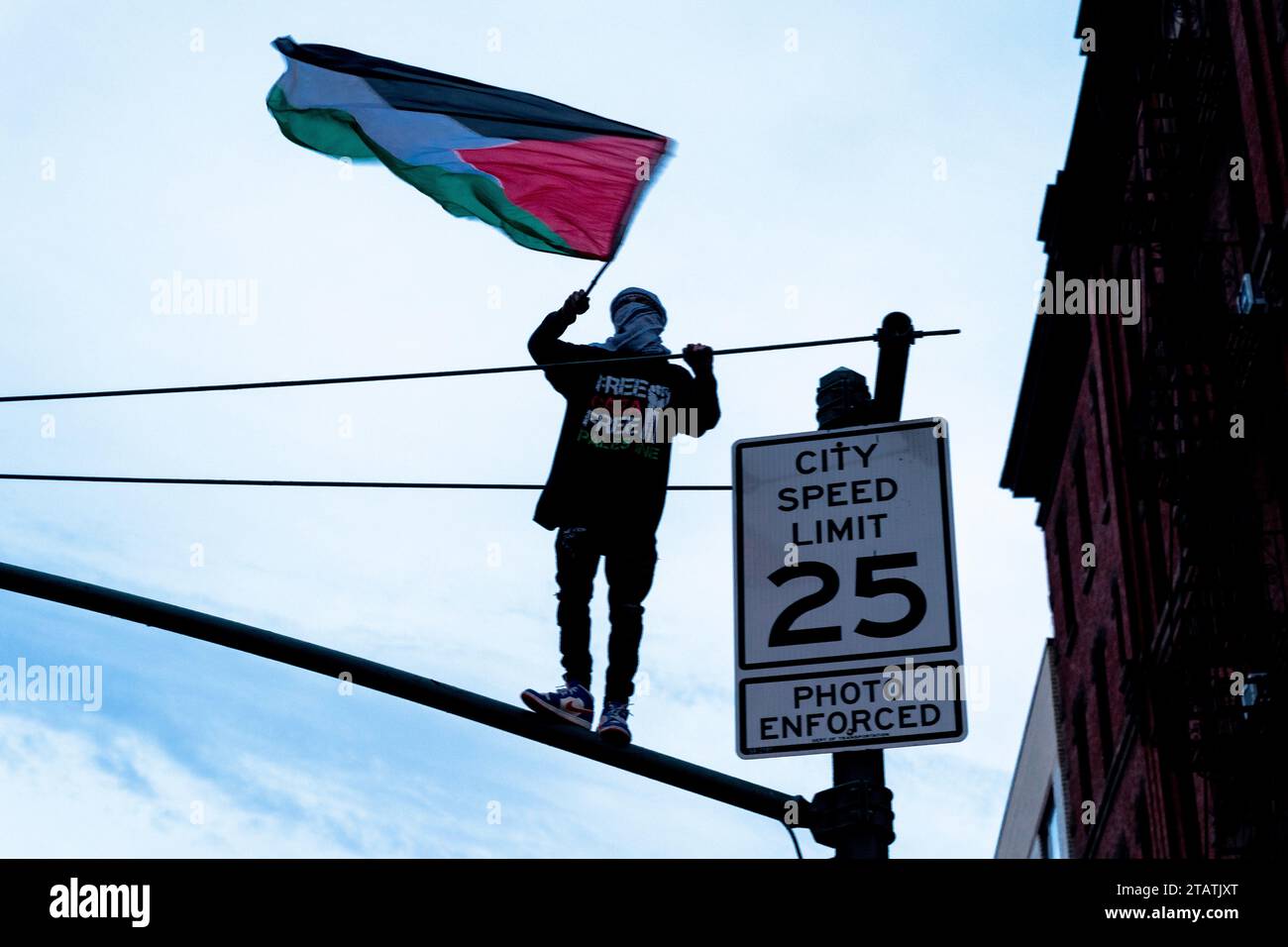 A man waving Palestinian flag while standing on top of ttraffic light ...