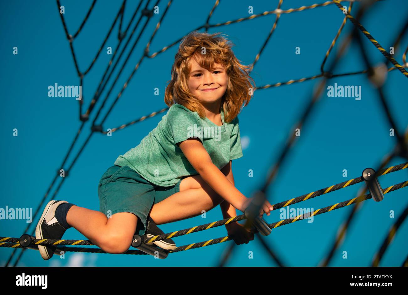 Cute smiling kid climbing the net at the playground. Kids rope park ...