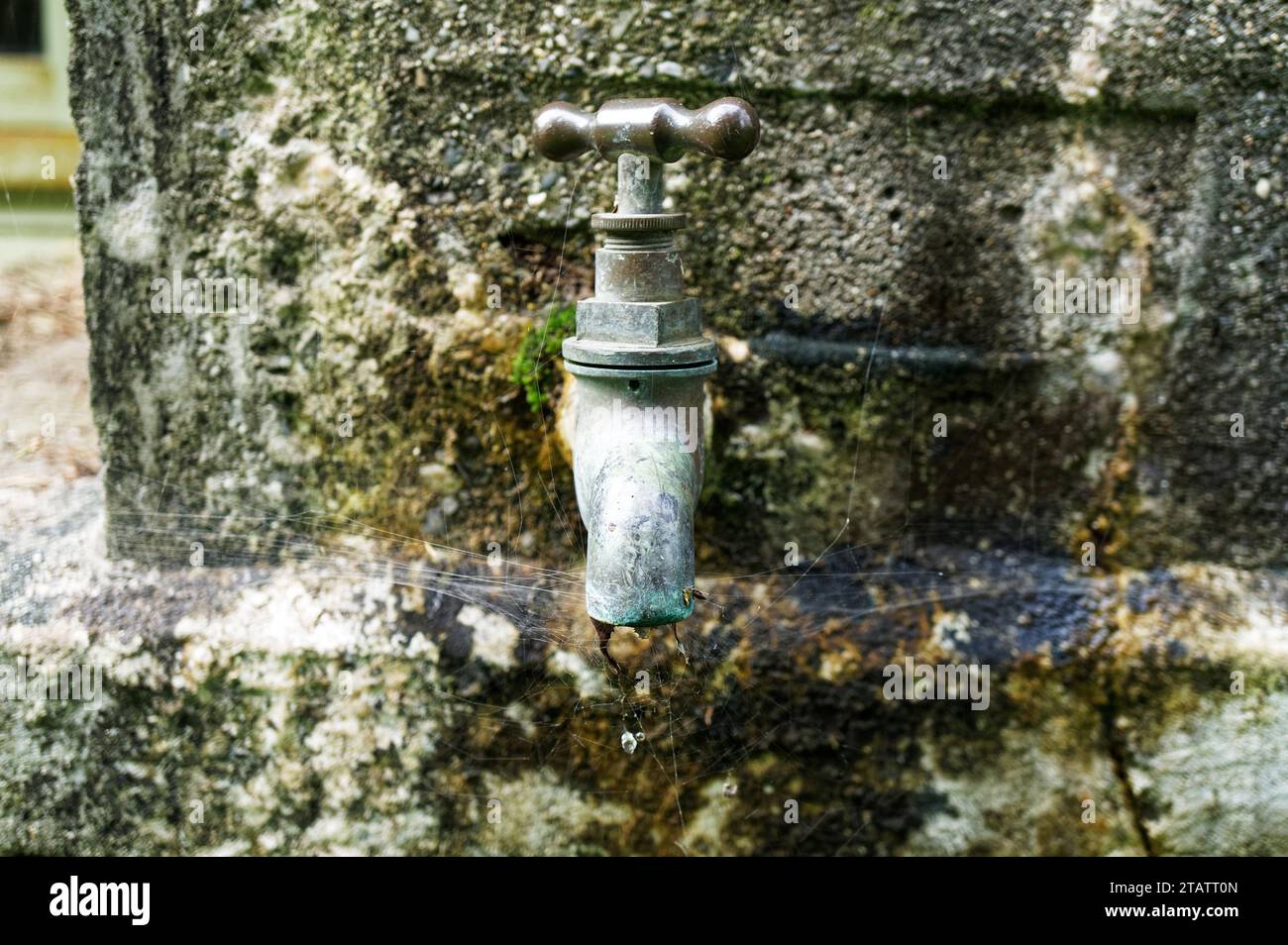 An old water tank has a dripping tap attached to it. A water droplet ...