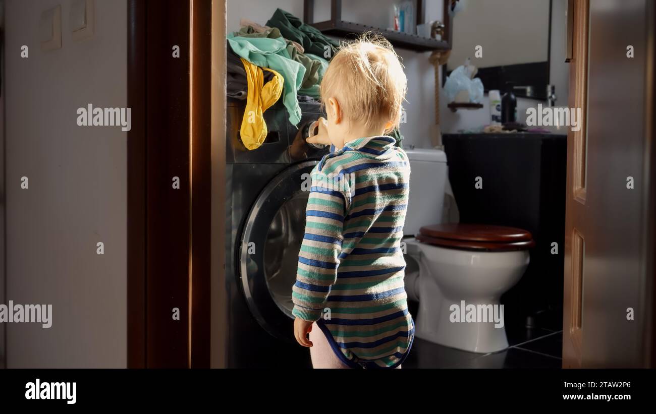 Little baby boy pressing knobs and buttons on working washing machine ...