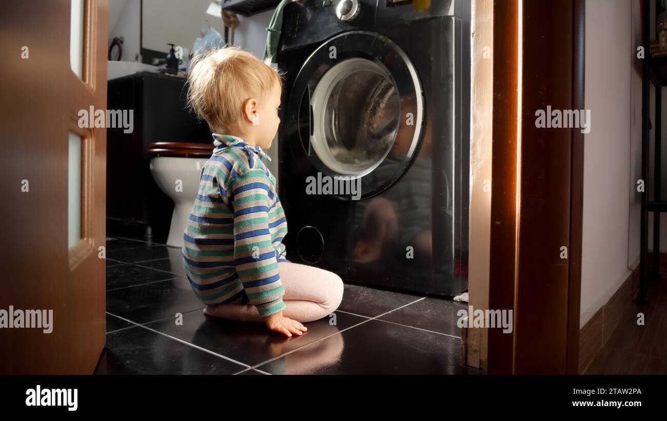 Cute baby boy looking at washing machine doing laundry. Doing housework ...
