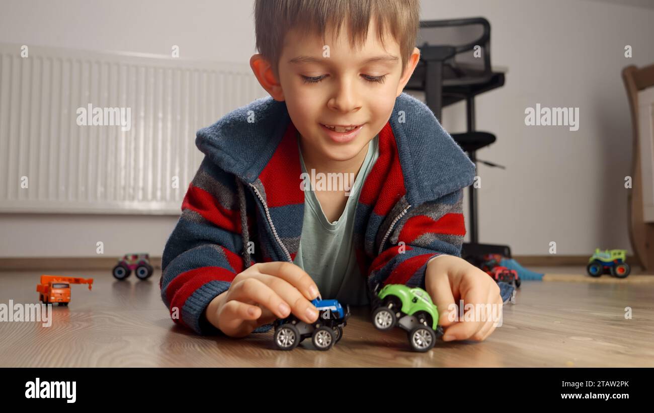 Portrait of cute boy lying on floor and playing with two toy cars ...
