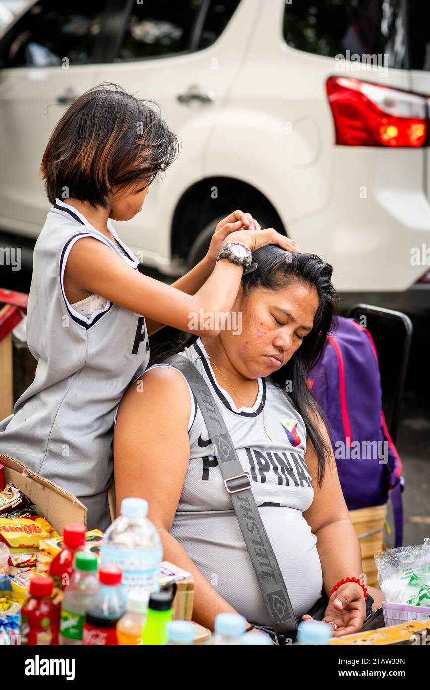 A Young Filipino Girl Cleans Her Mothers Hair Sat At Their Street Stall