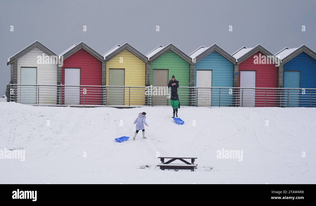 People walk through the snow beside the beach huts at Blyth in ...