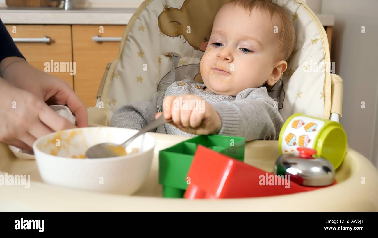 Portrait of mother wiping with paper towel her messy baby boy eating ...