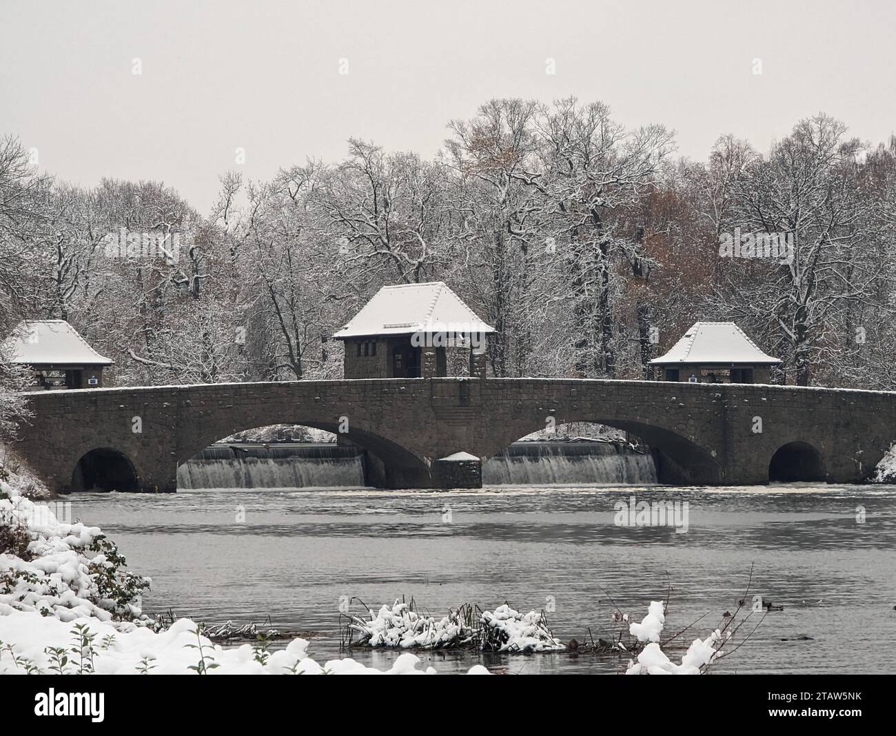 A scenic winter landscape featuring a bridge arching over a tranquil ...