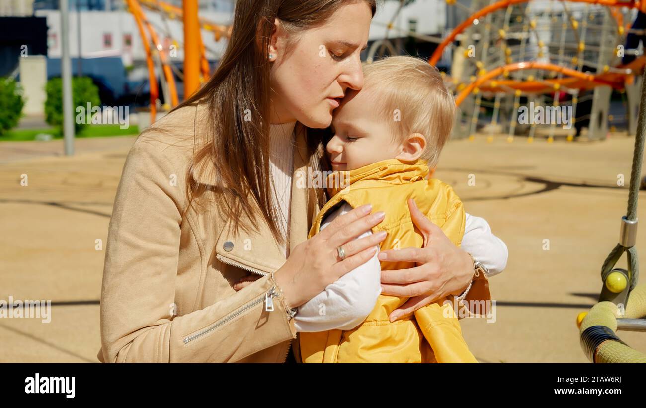 Young mother consoling and hugging her upset baby boy on playground ...