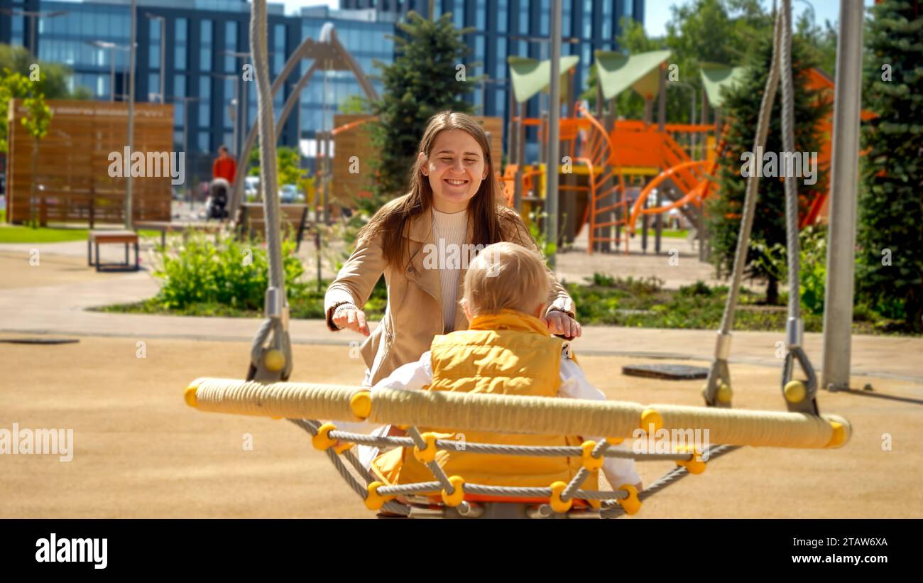 Happy smiling mother rocking her baby son swinging in swing on ...