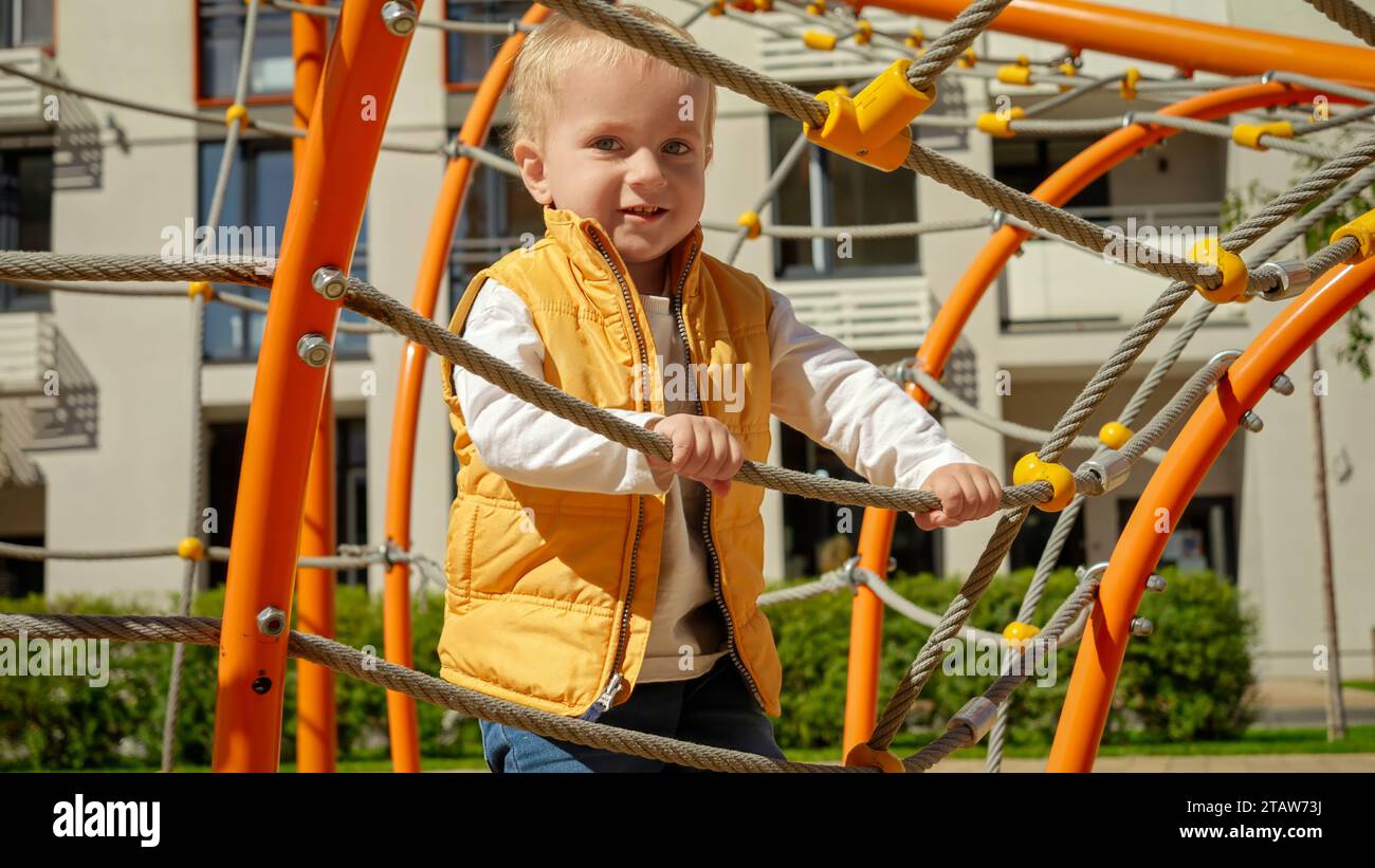 Cute baby boy standing on the rope spider web on the playground ...