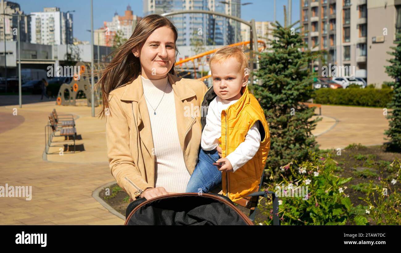 Beautiful smiling mother holding her baby son and walking with stroller ...
