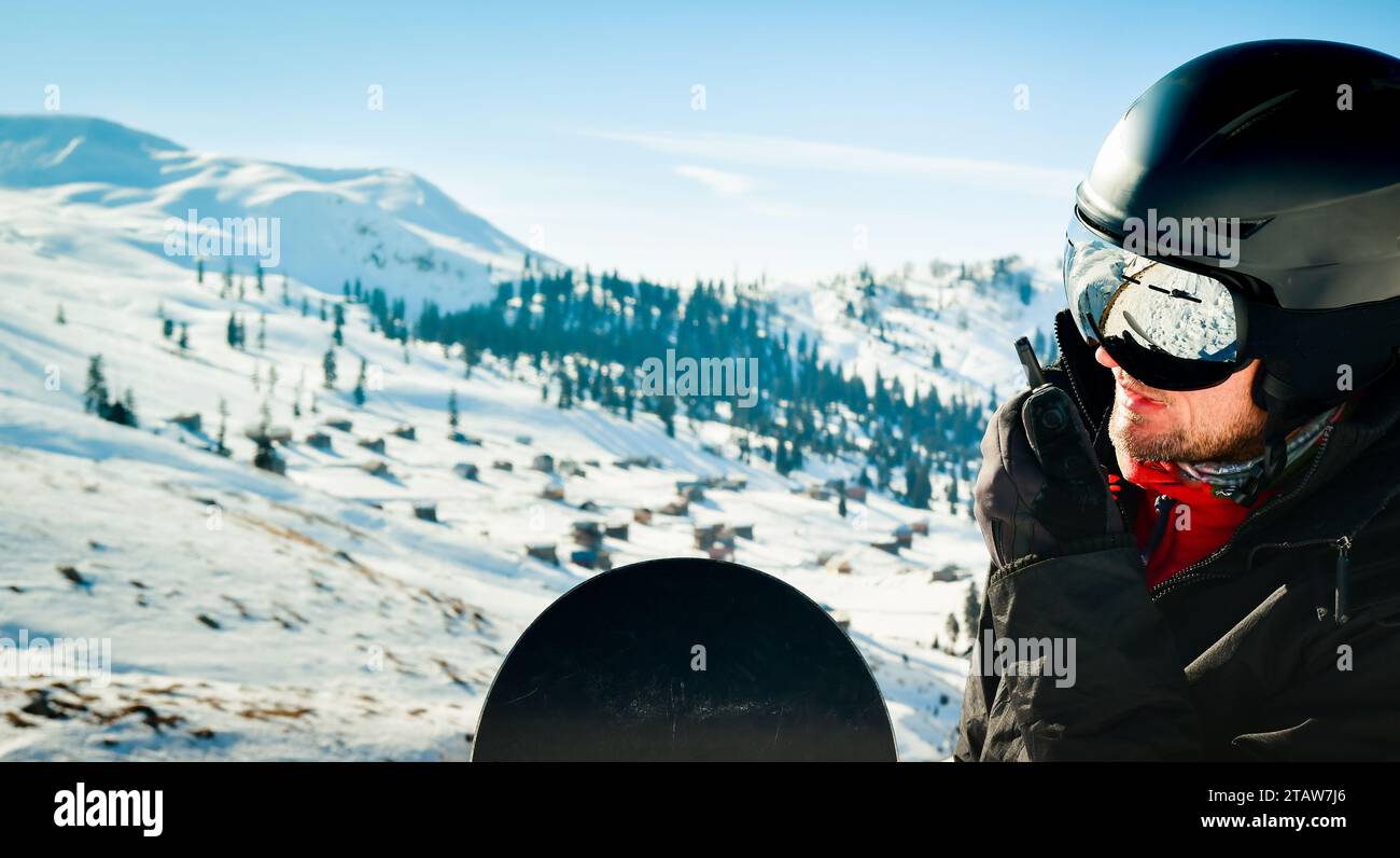 Portrait of bearded man snowboarder on walkie-talkie wear sunglasses and ski helmet for safety ...
