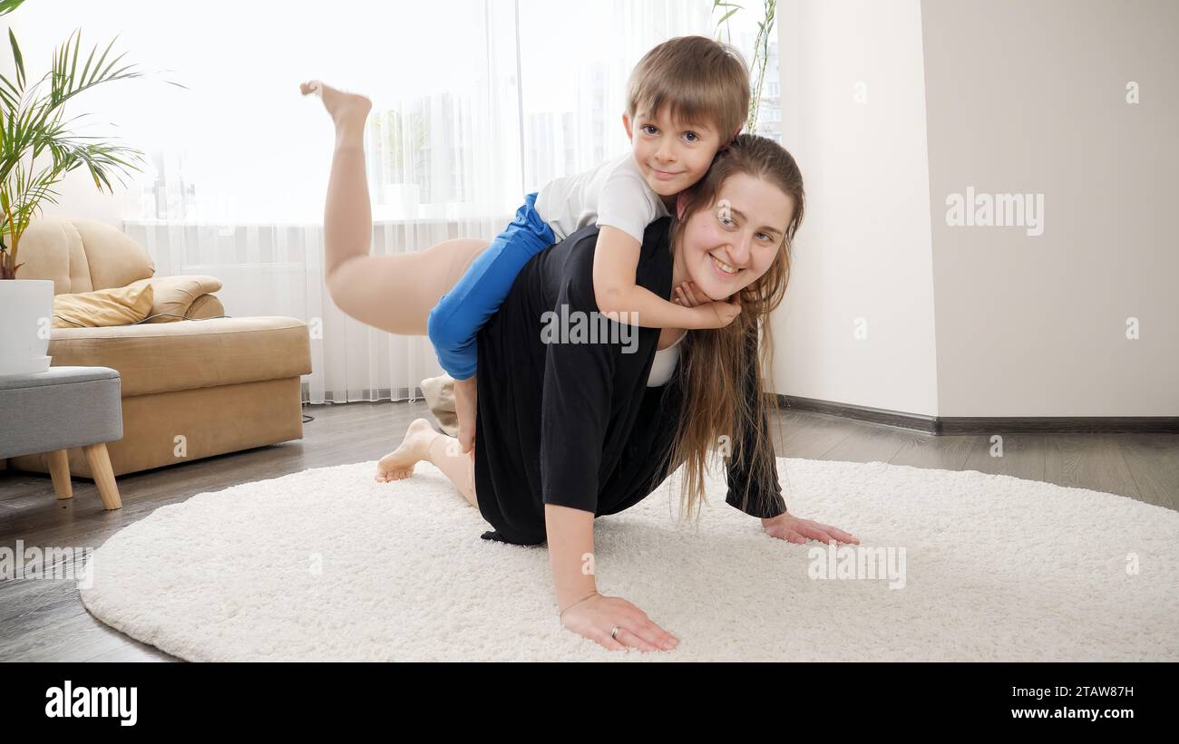 Little boy riding on mothers back while she is doing fitness exercises ...