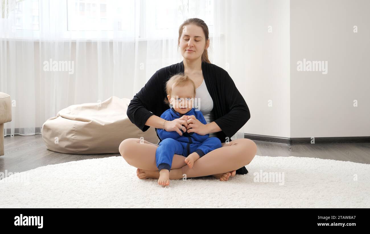 Happy smiling young mother teaching her little baby son doing yoga ...