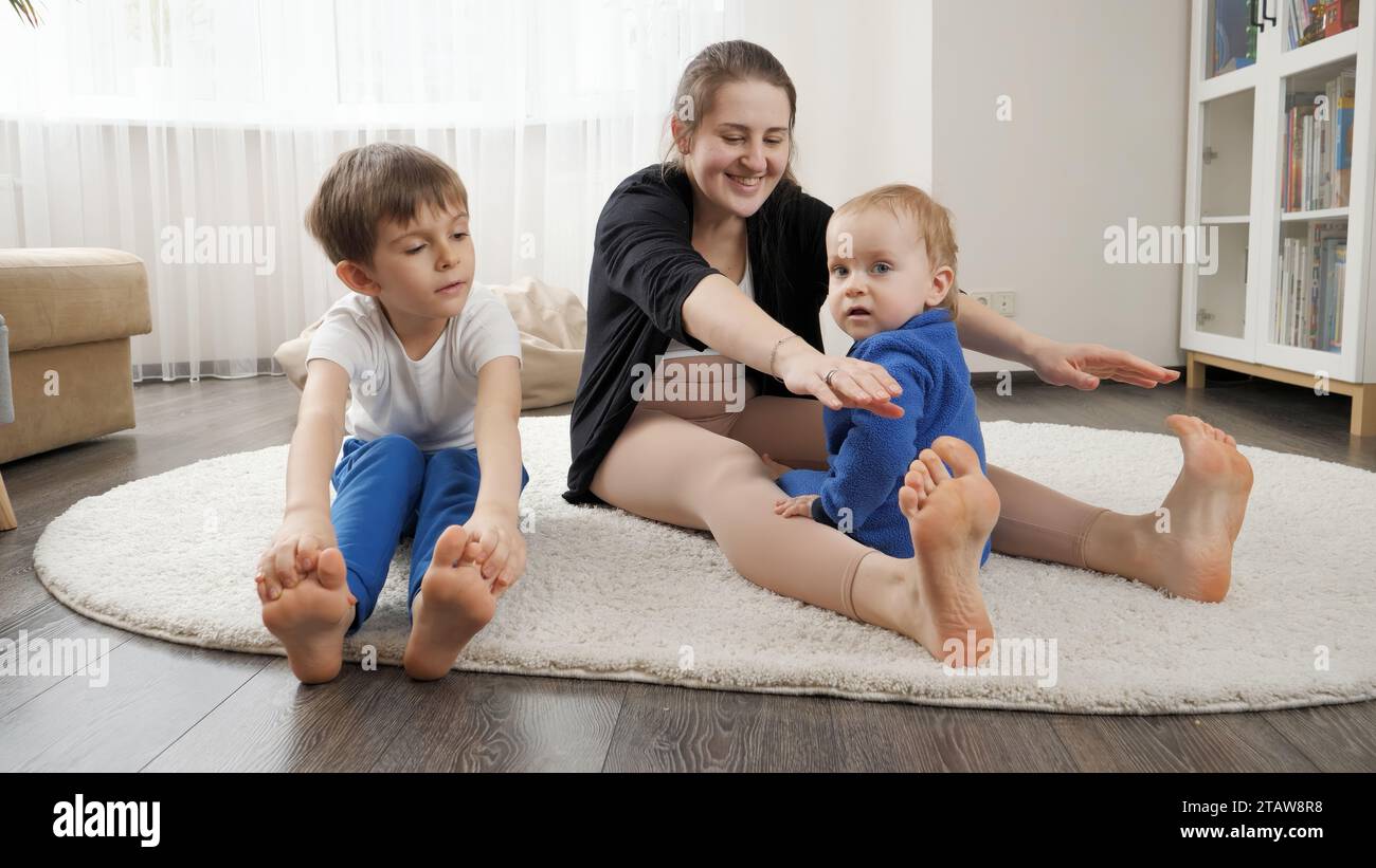 Young mother with her baby and older son doing stretching and fitness ...