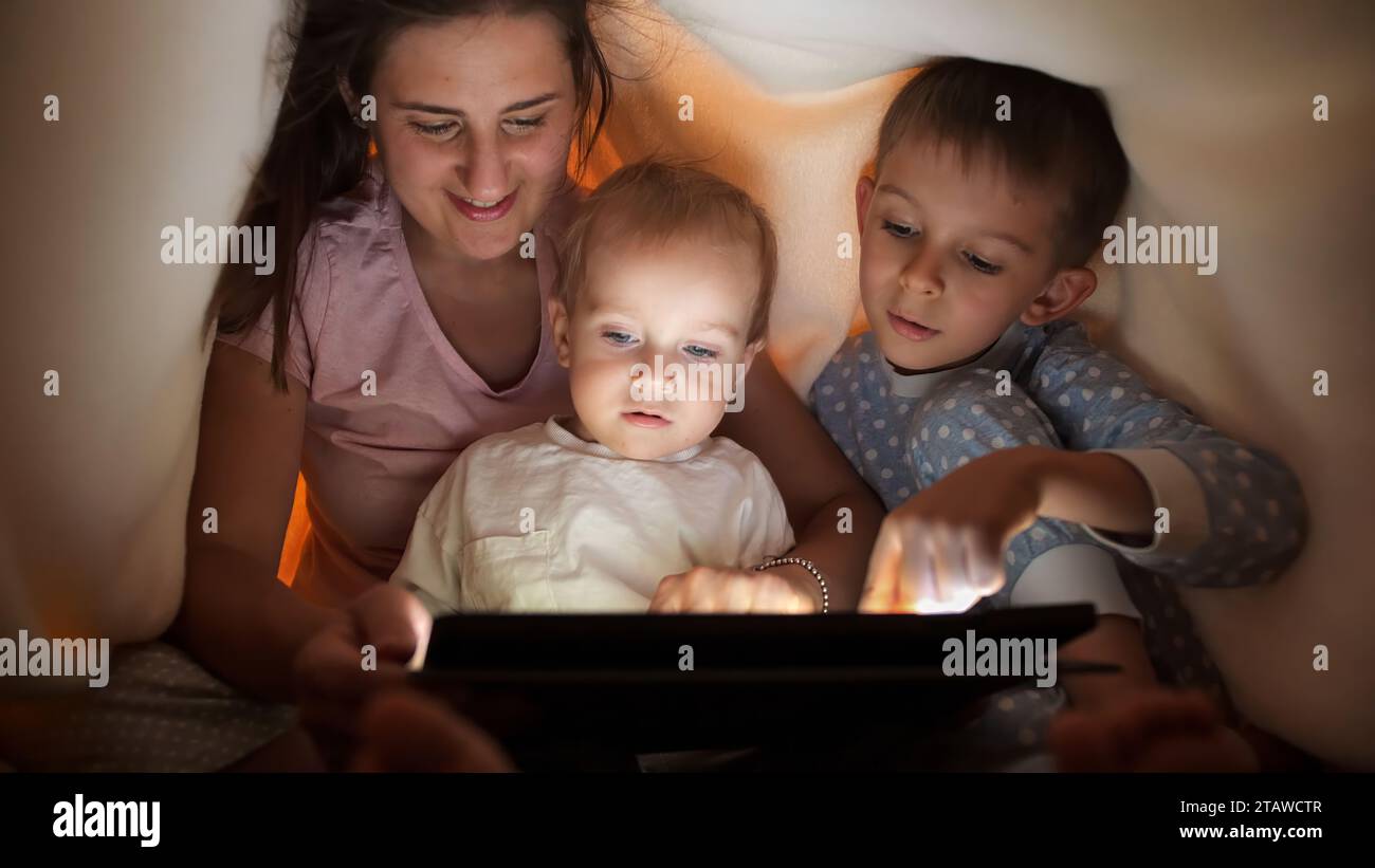 Happy cheerful family hiding under blanket and using tablet computer ...