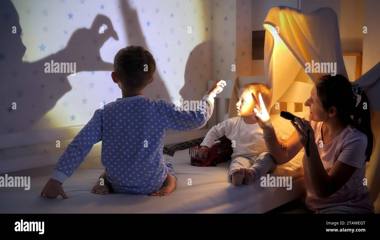 Young mother playing with flashlight and her two sons showing them ...