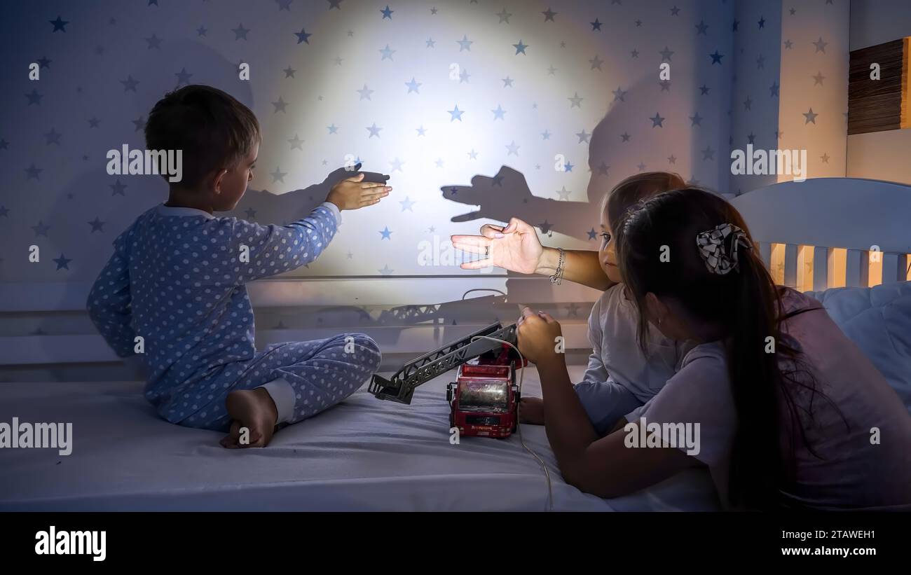 Happy kids with mother playing with flashlight in shadow theater at ...
