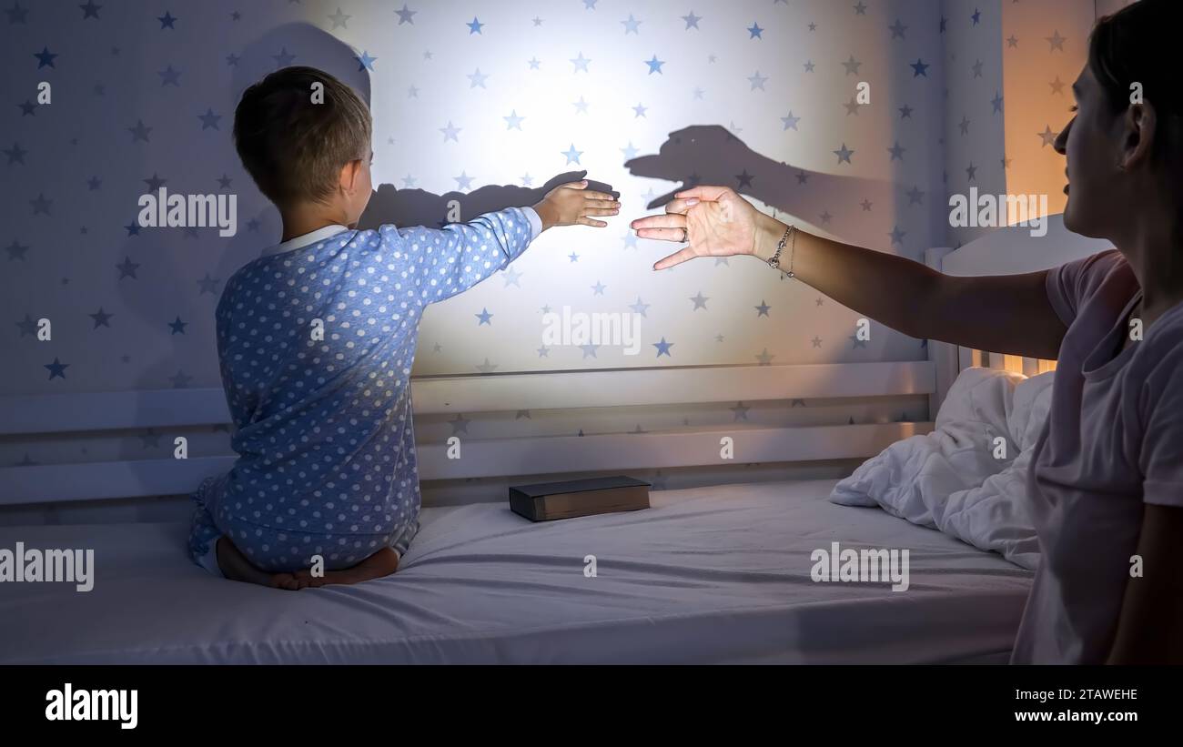 Cute boy with mother in pajamas playing with shadows on wall from the ...