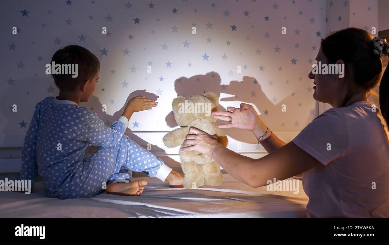 Smiling boy with mother showing theater of shadows with flashlight on ...