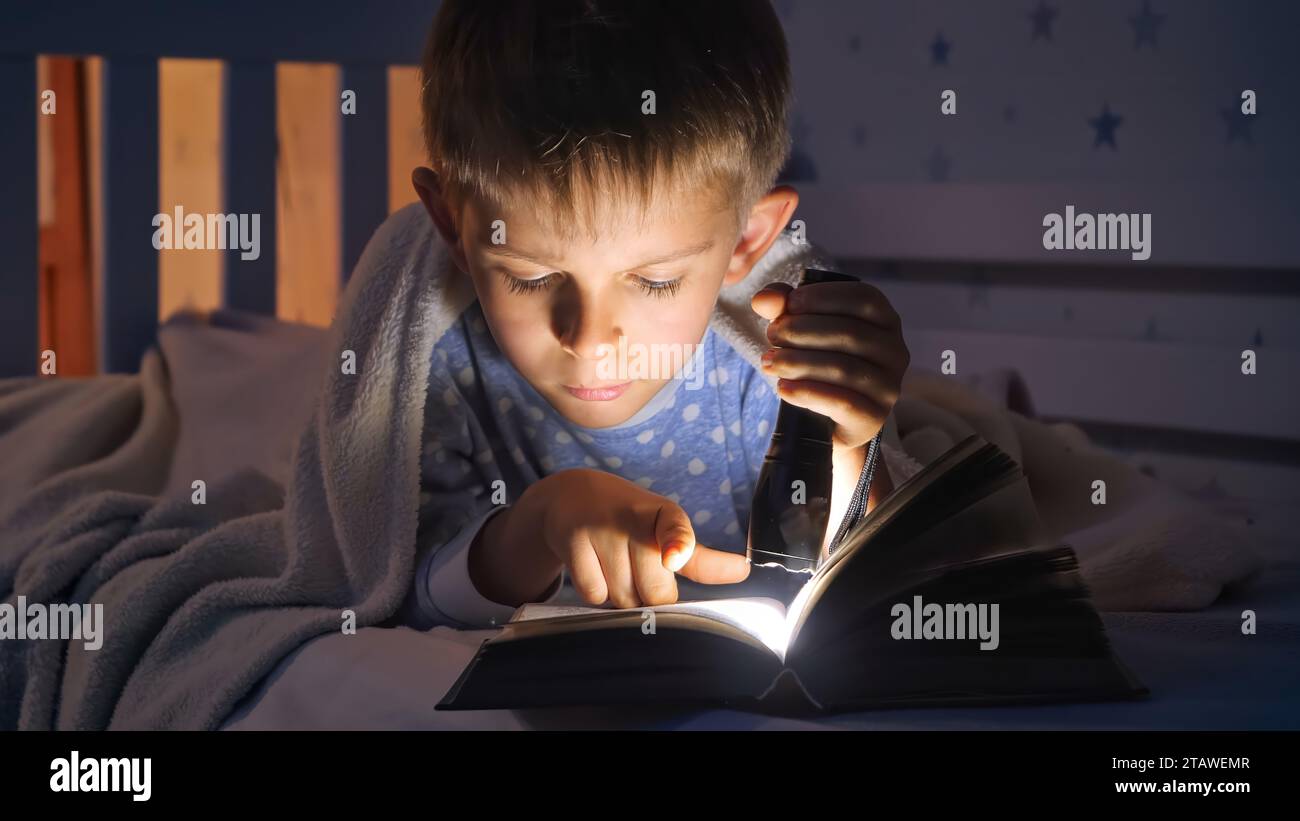 Portrait of smiling boy reading books before going to sleep at night ...