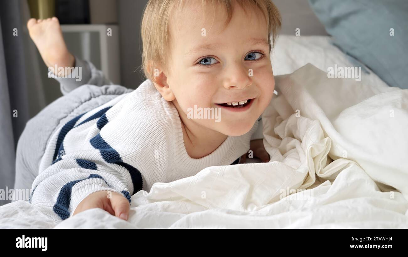 Cheerful smiling toddler boy relaxing in bed at morning. Happy kids ...