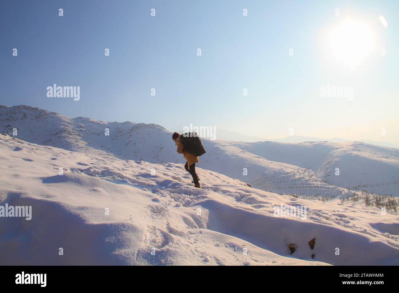 A young man hiking on top of snowy mountains during the winter season ...