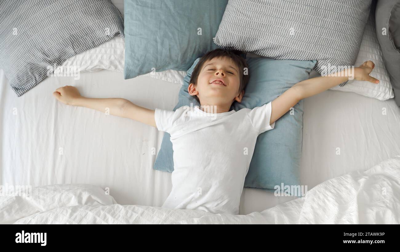 Cute little boy lying in bed, stretching hands and yawn. Child waking up in bed at morning Stock ...